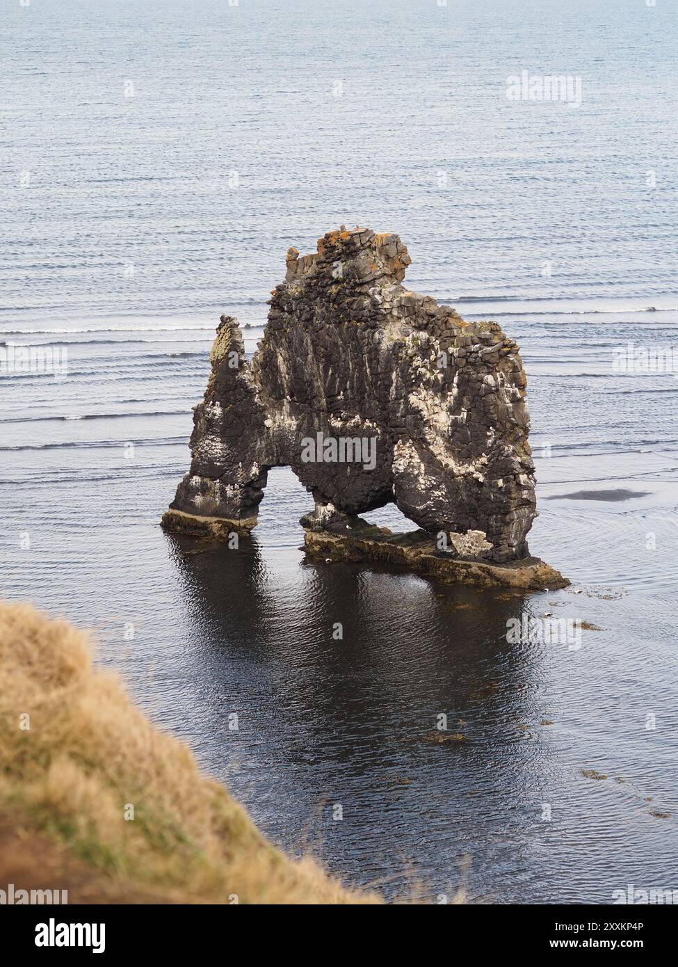 A unique rock formation rising from the calm sea, adorned with natural ...