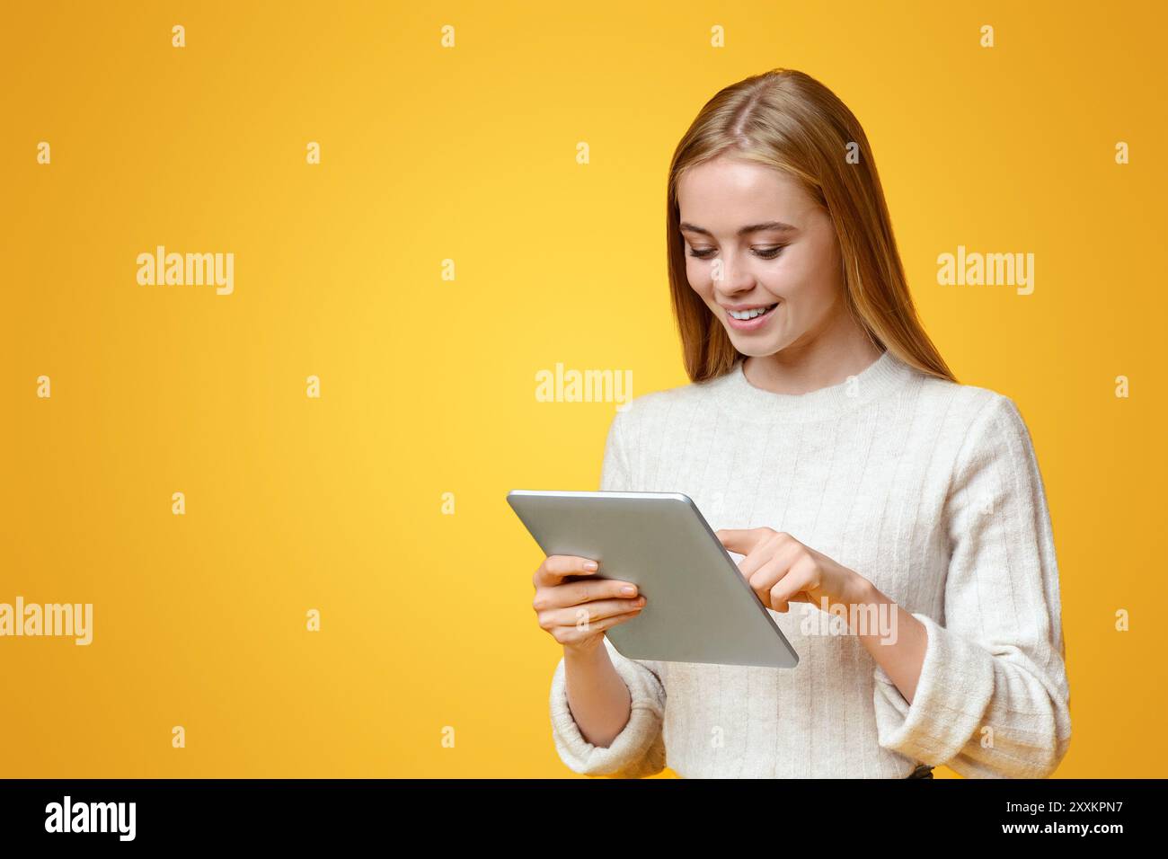 Beautiful teen girl using digital tablet over orange studio background ...