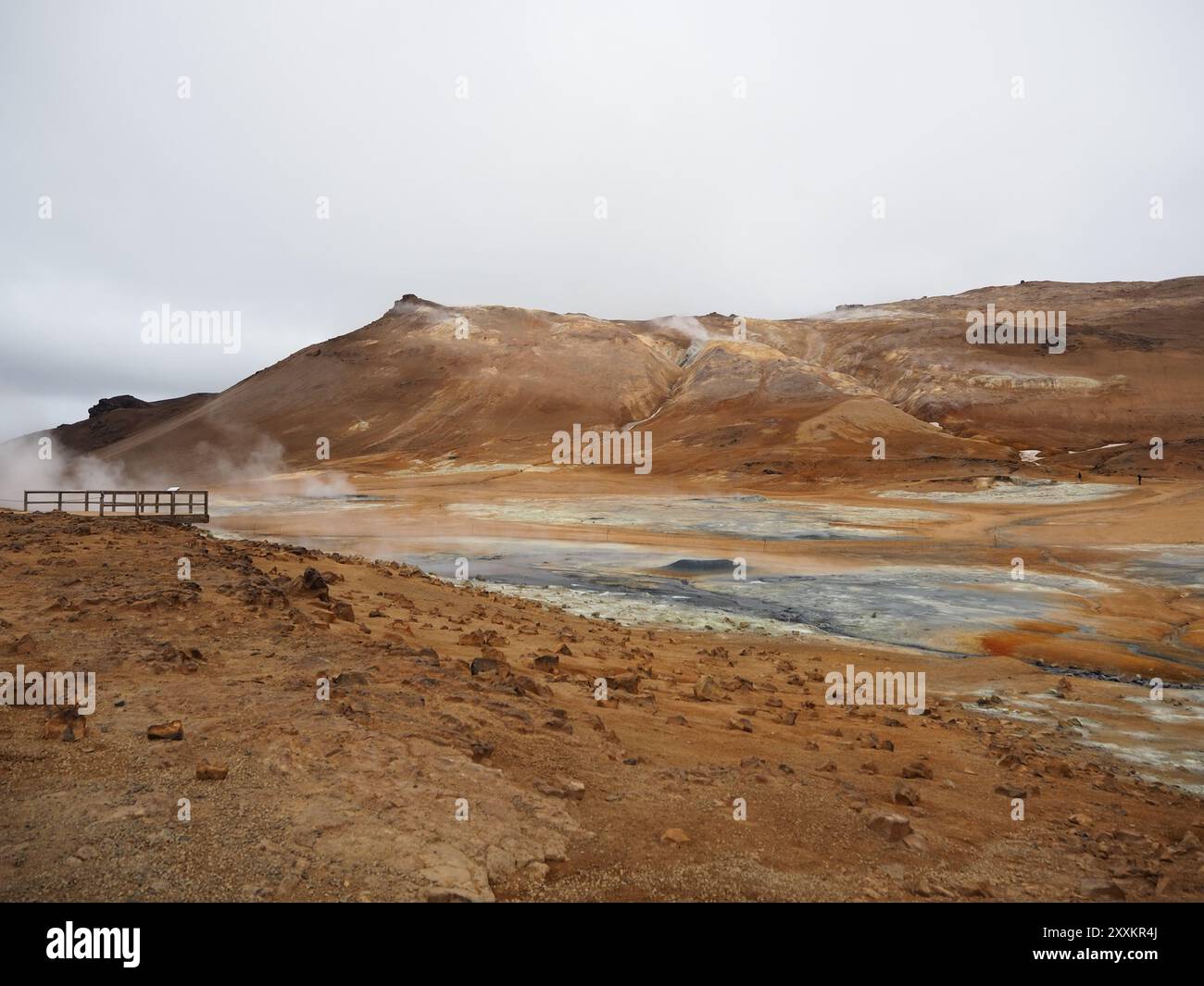A barren geothermal landscape with steaming vents and surrounding hills ...