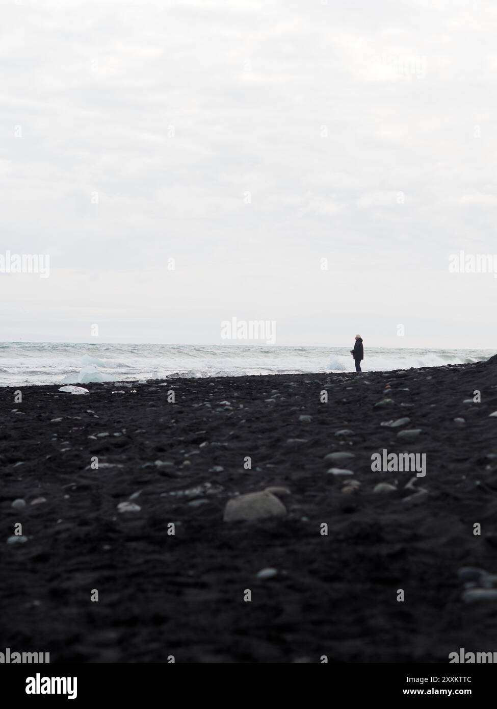 A solitary person stands on the vast black sand shore, gazing towards ...