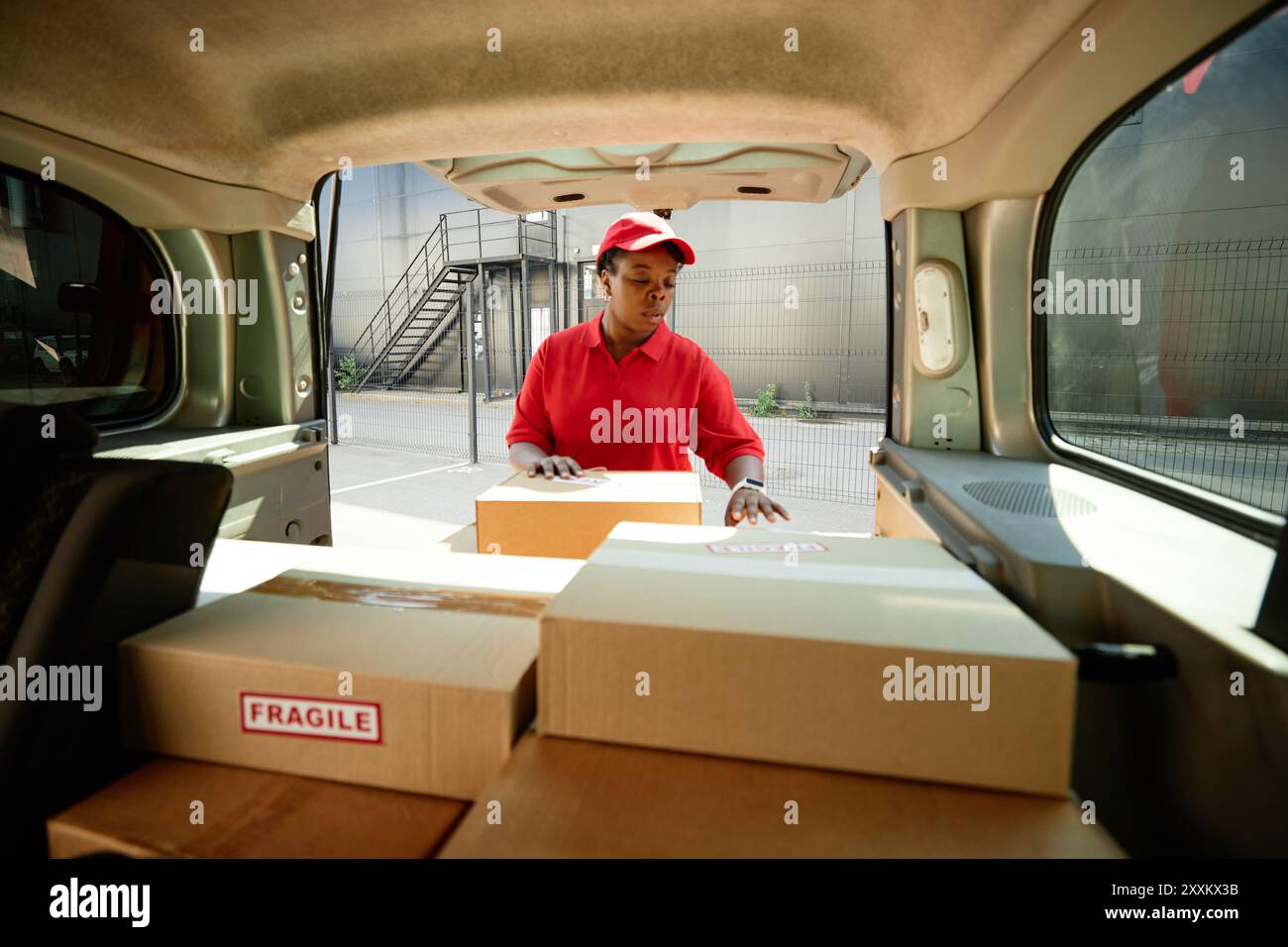 Delivery worker wearing red uniform unloading packages from back of van ...