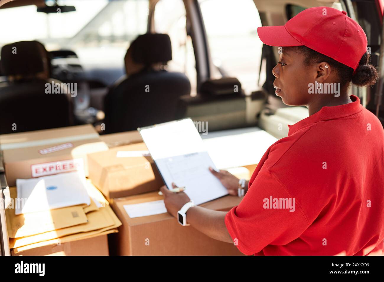 Woman in red shirt and cap organizing packages in vehicle, preparing ...