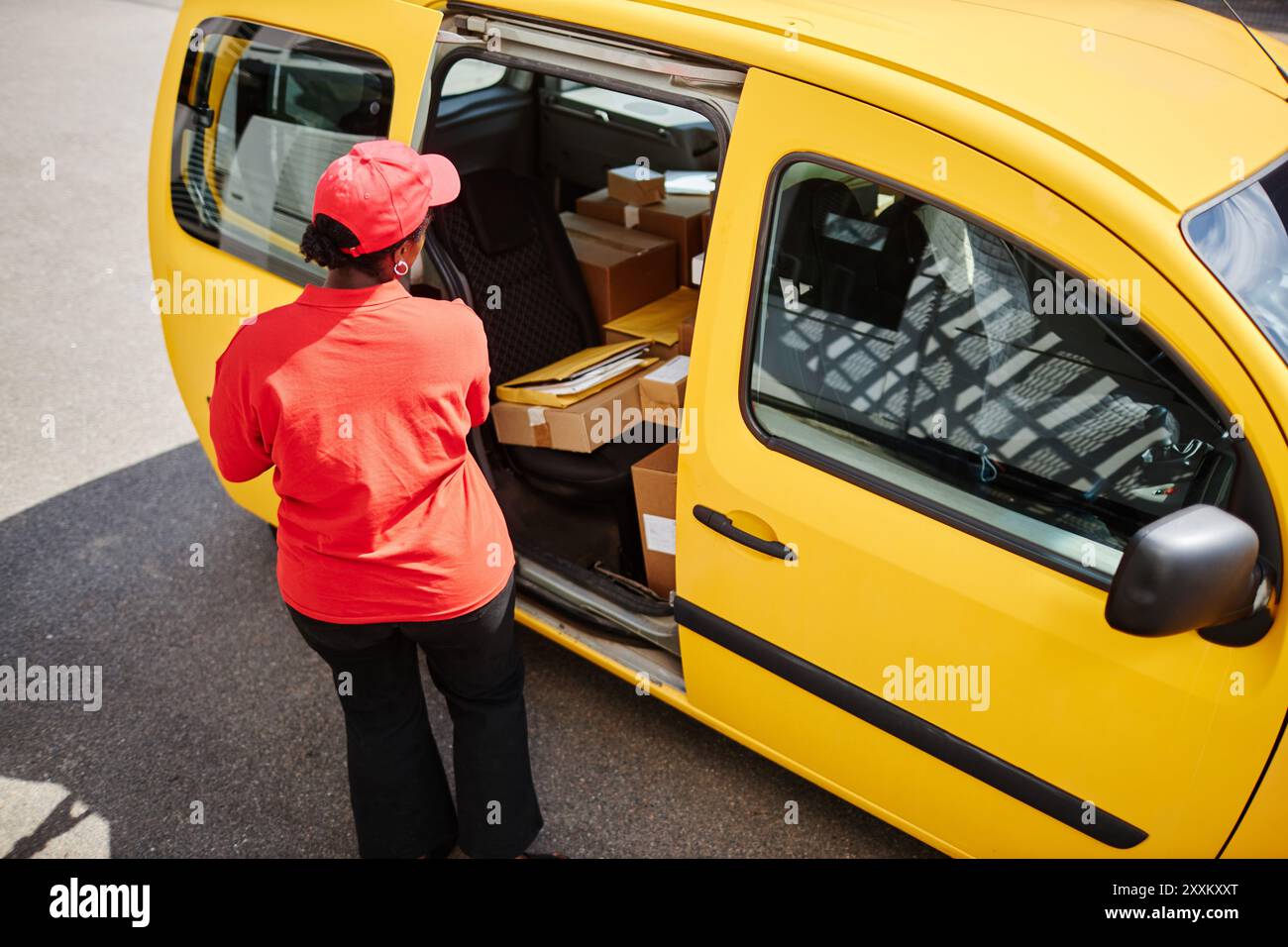 Worker in red uniform loading packages into a yellow delivery van ...