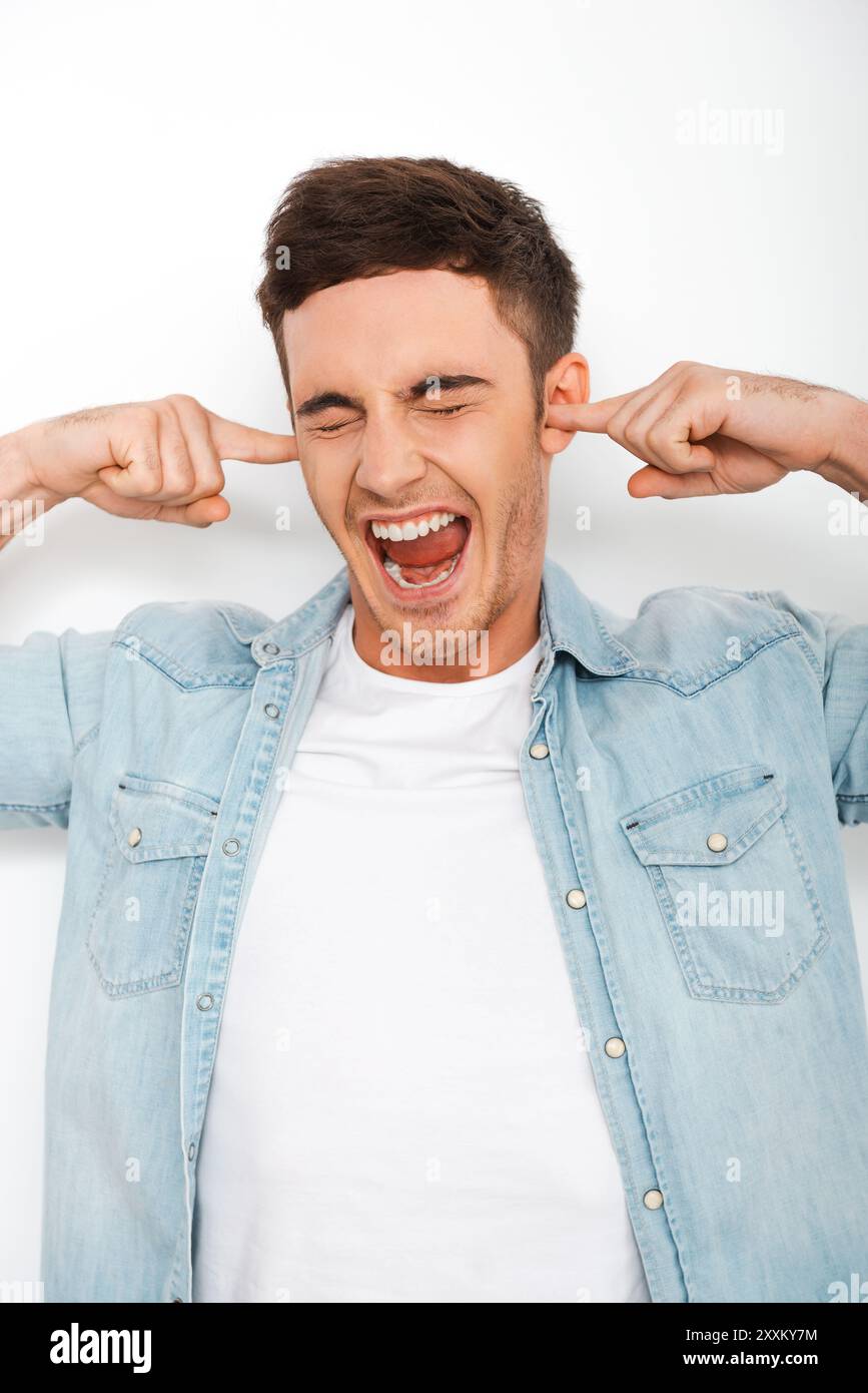 Stop it! Frustrated young man holding fingers in ears and screaming ...