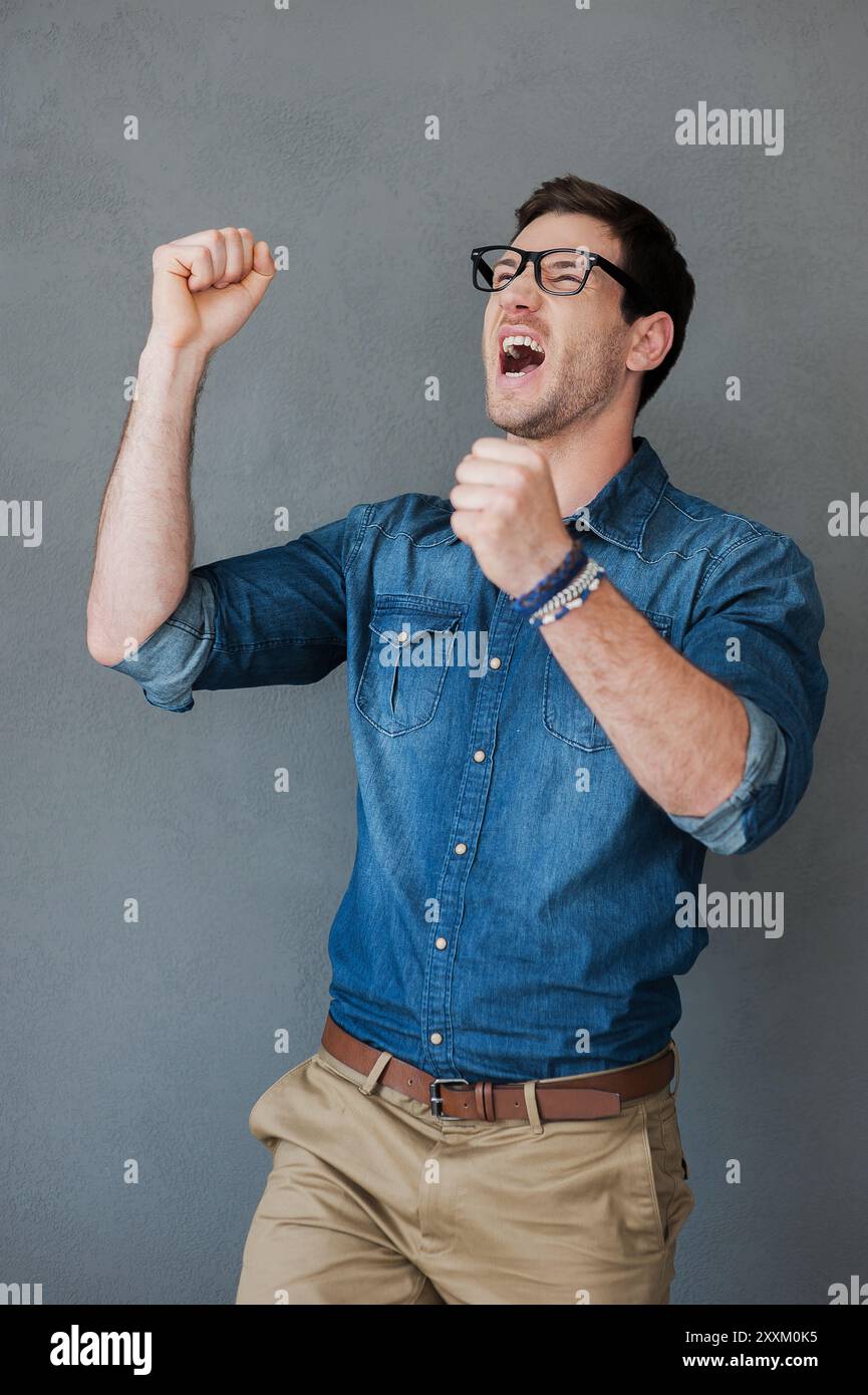Celebrating success. Excited young man keeping arms raised and ...