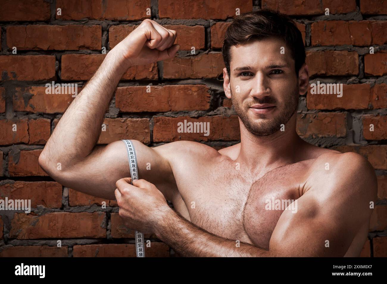 Measuring his perfect bicep. Smiling muscular man measuring his bicep ...