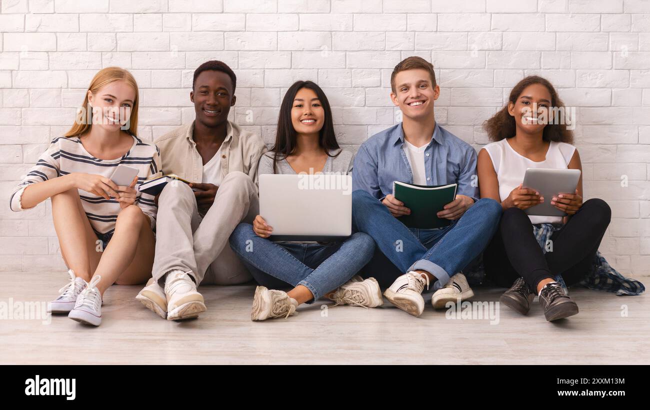 Smiling group of international students studying over white brick wall ...