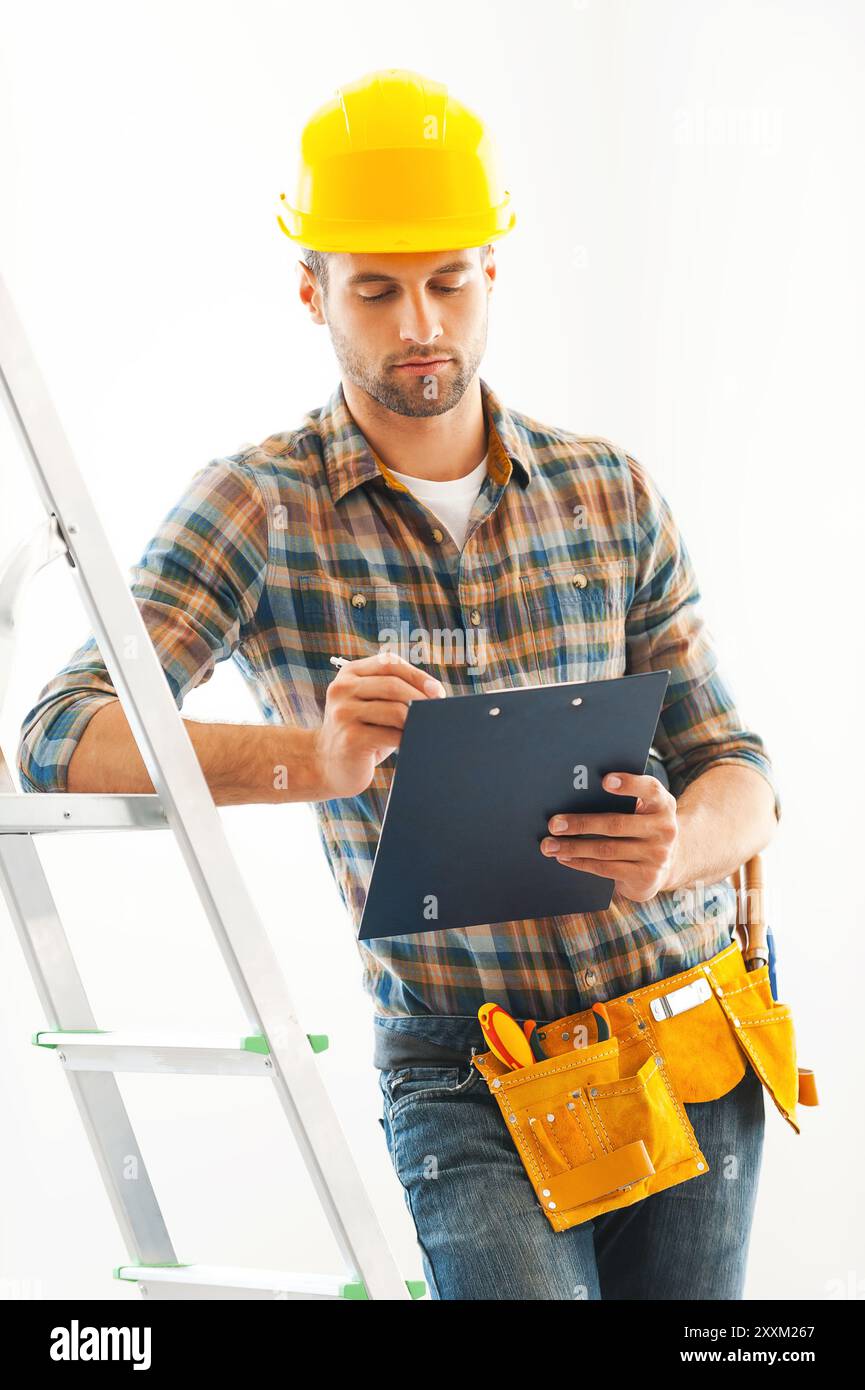 Master of building at work. Serious young builder writing in clipboard ...