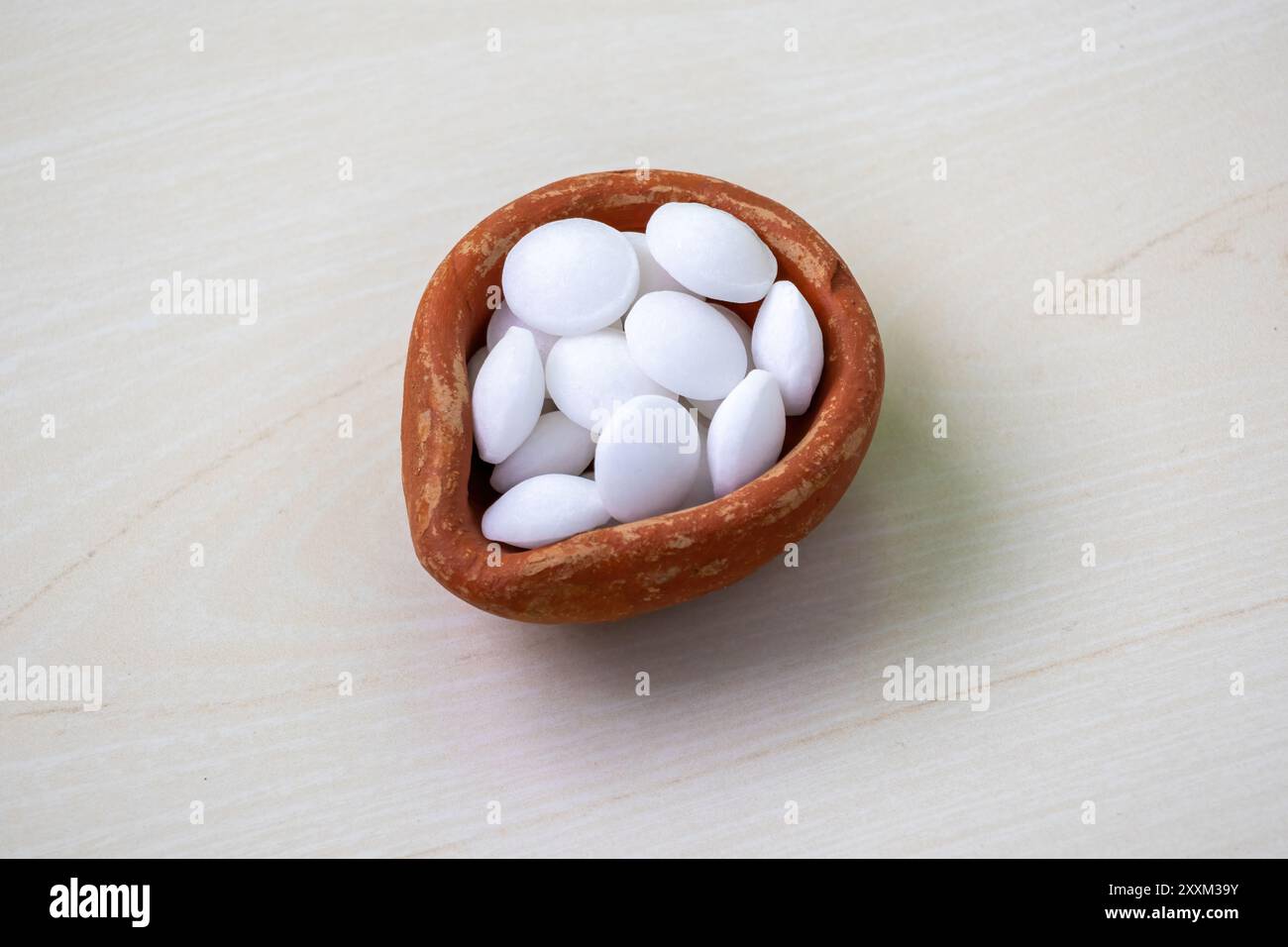 An earthen pot full of white naphthalene balls on wooden background. It ...