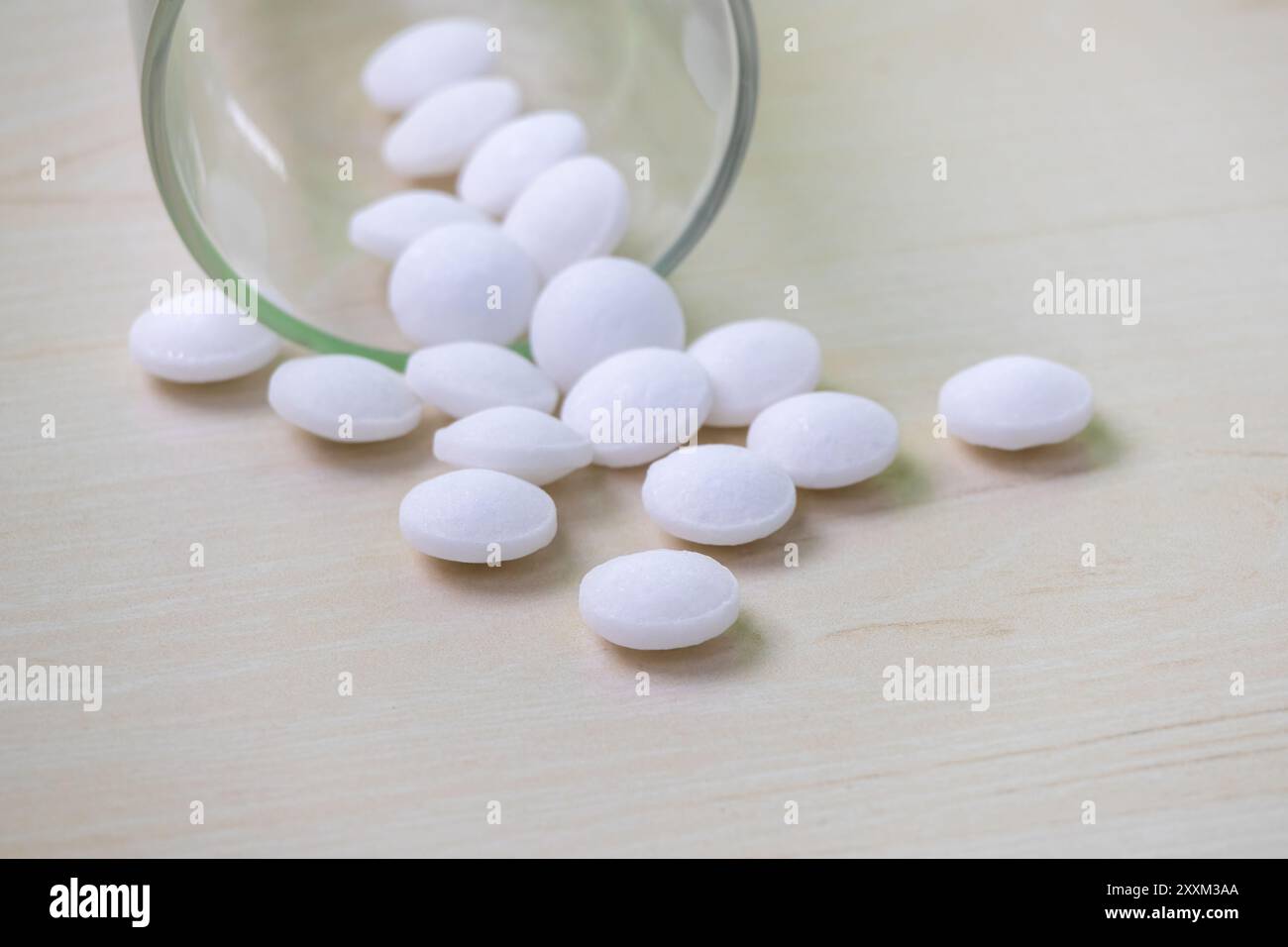 Many white naphthalene mothballs spilled from a glass on a light wooden ...