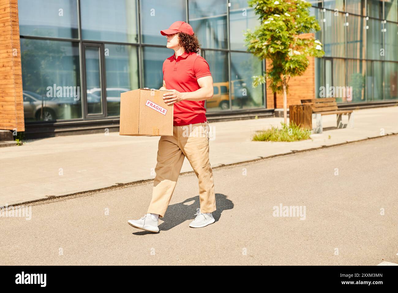 Delivery person wearing red uniform holding cardboard package labeled ...