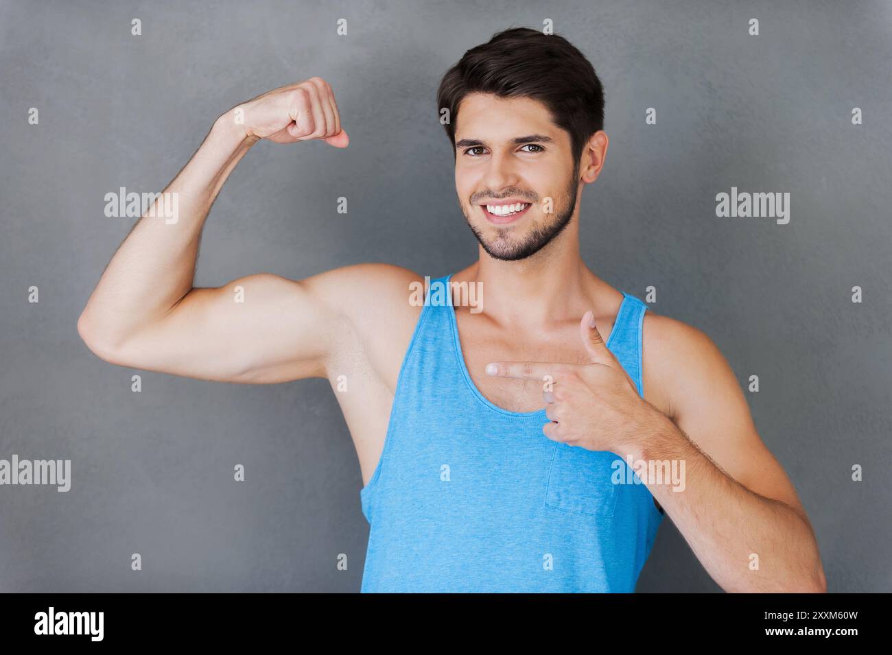 Proud of his perfect biceps. Cheerful young muscular man pointing his ...
