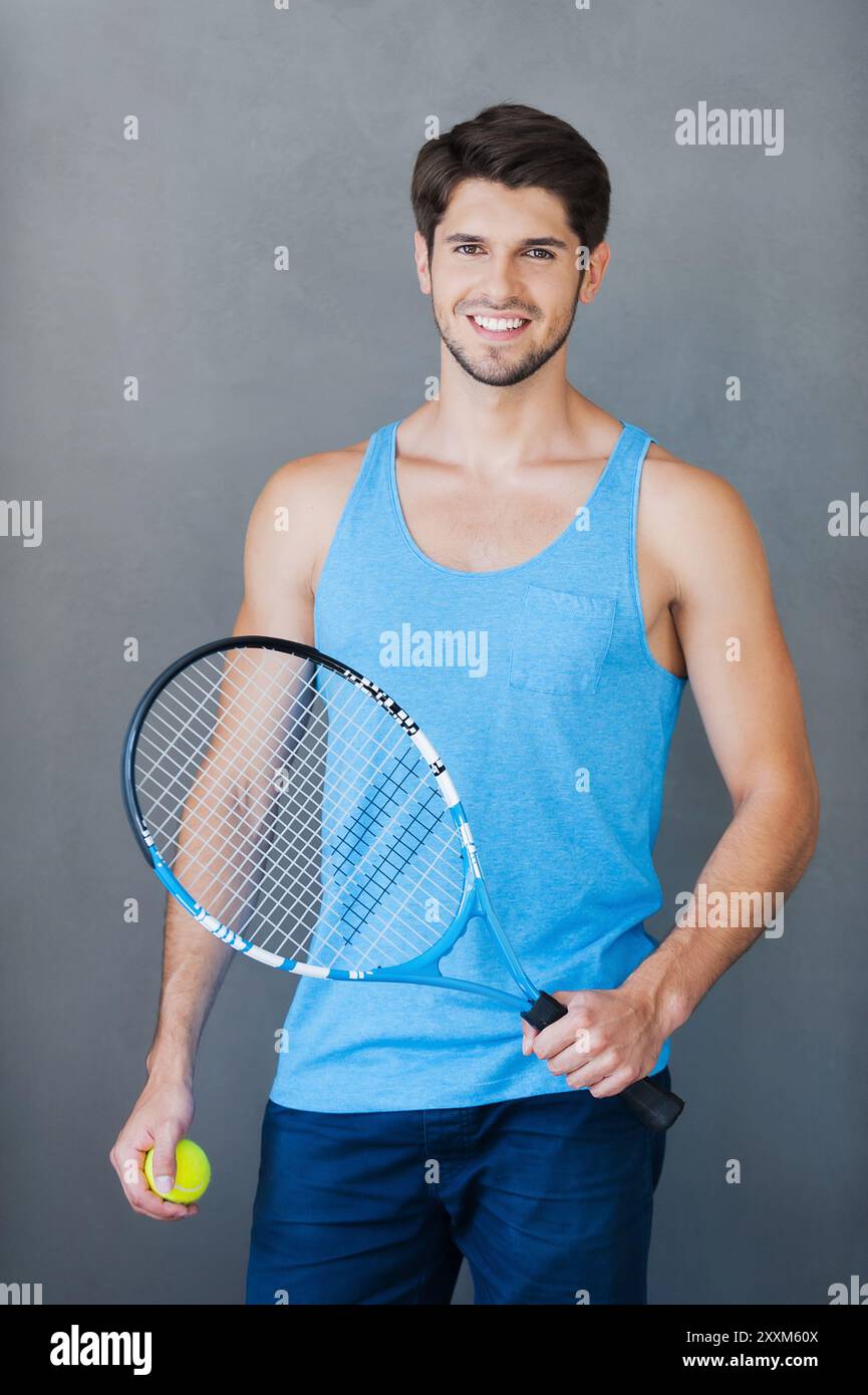 Ready to play. Smiling young muscular man holding tennis racket while ...