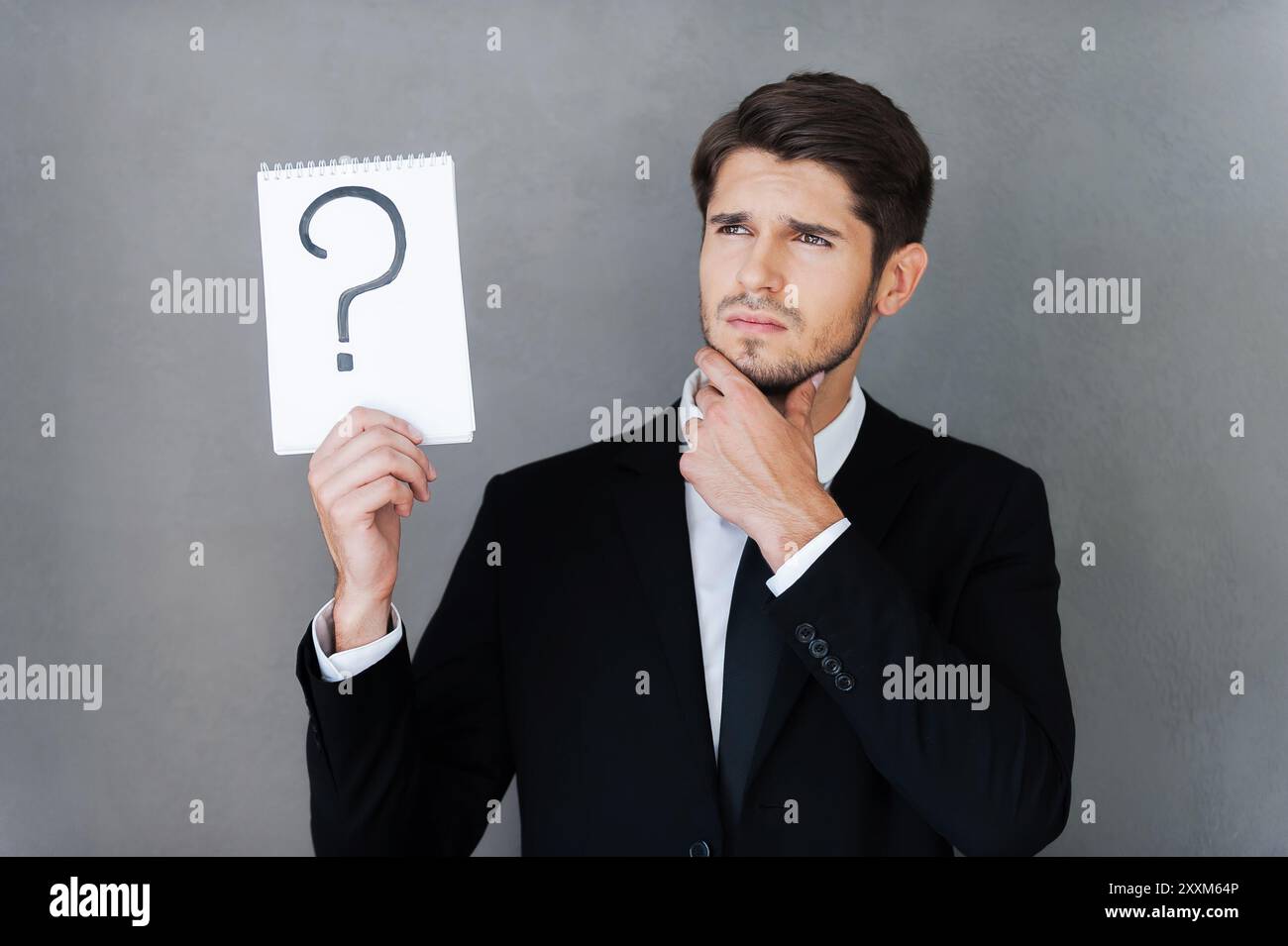 In search of answer. Thoughtful young businessman holding note pad with ...