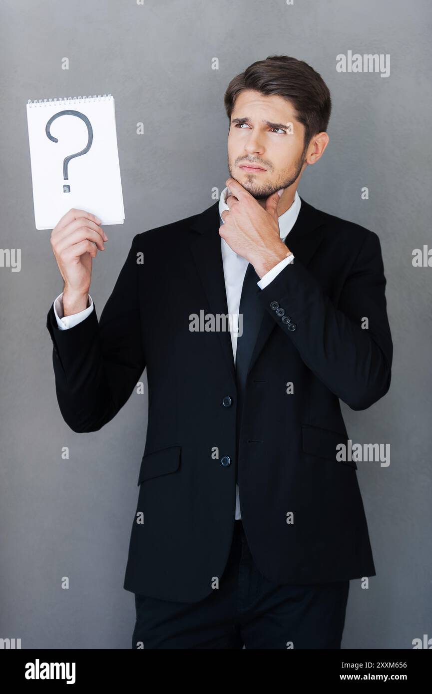 He has big question. Thoughtful young businessman holding note pad with ...