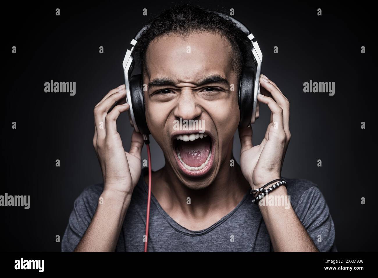 Too loud sound. Furious young African man adjusting headphones and looking at camera with mouth ...