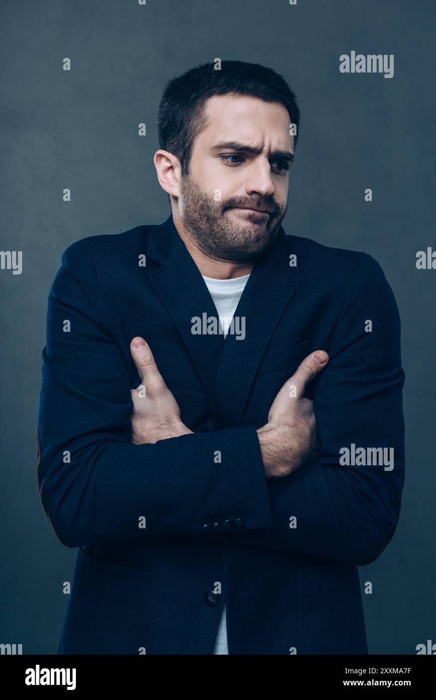 Feeling uncertain. Confused young man crossing his hands and grimacing ...