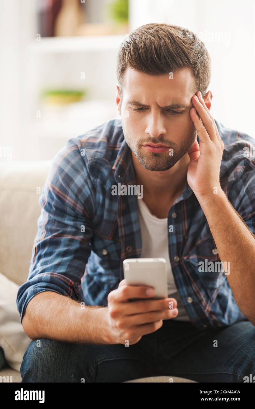 Dealing with bad news. Frustrated young man holding mobile phone and ...