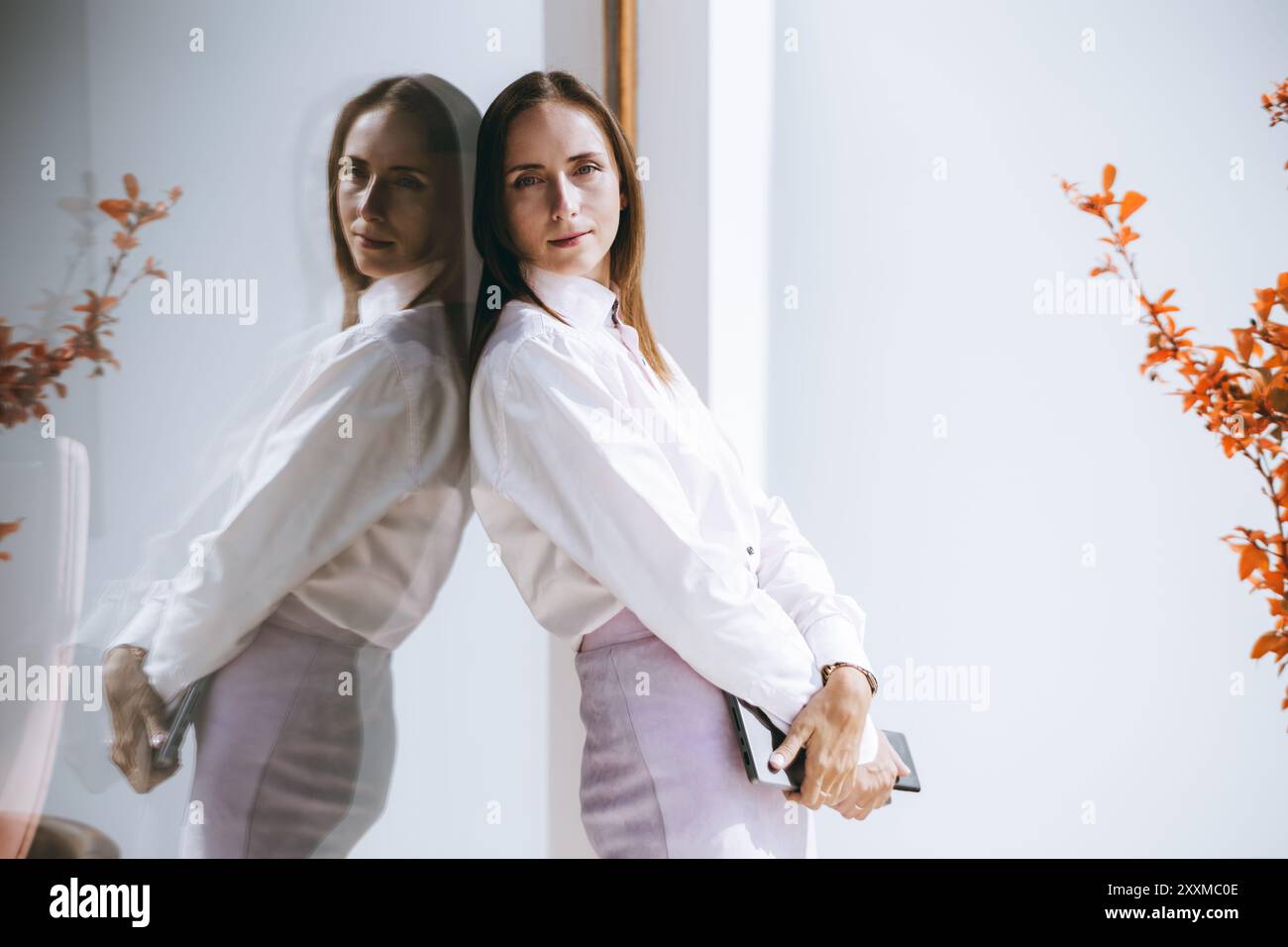 A professional woman in a white blouse and light skirt leans against a ...