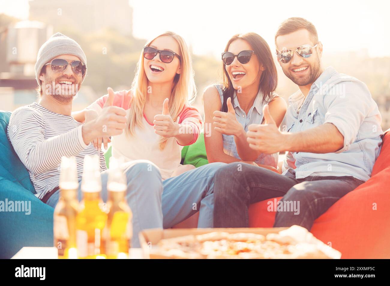 Enjoying good time. Four young cheerful people showing their thumbs up ...
