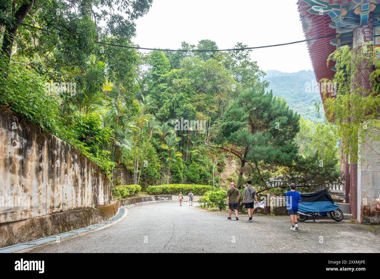 Visitors to Kek Lok Si Temple walk downhill along a road as they walk ...