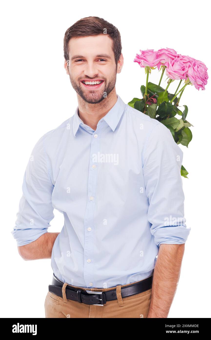 Surprise for her. Handsome young man hiding a bouquet with pink roses ...