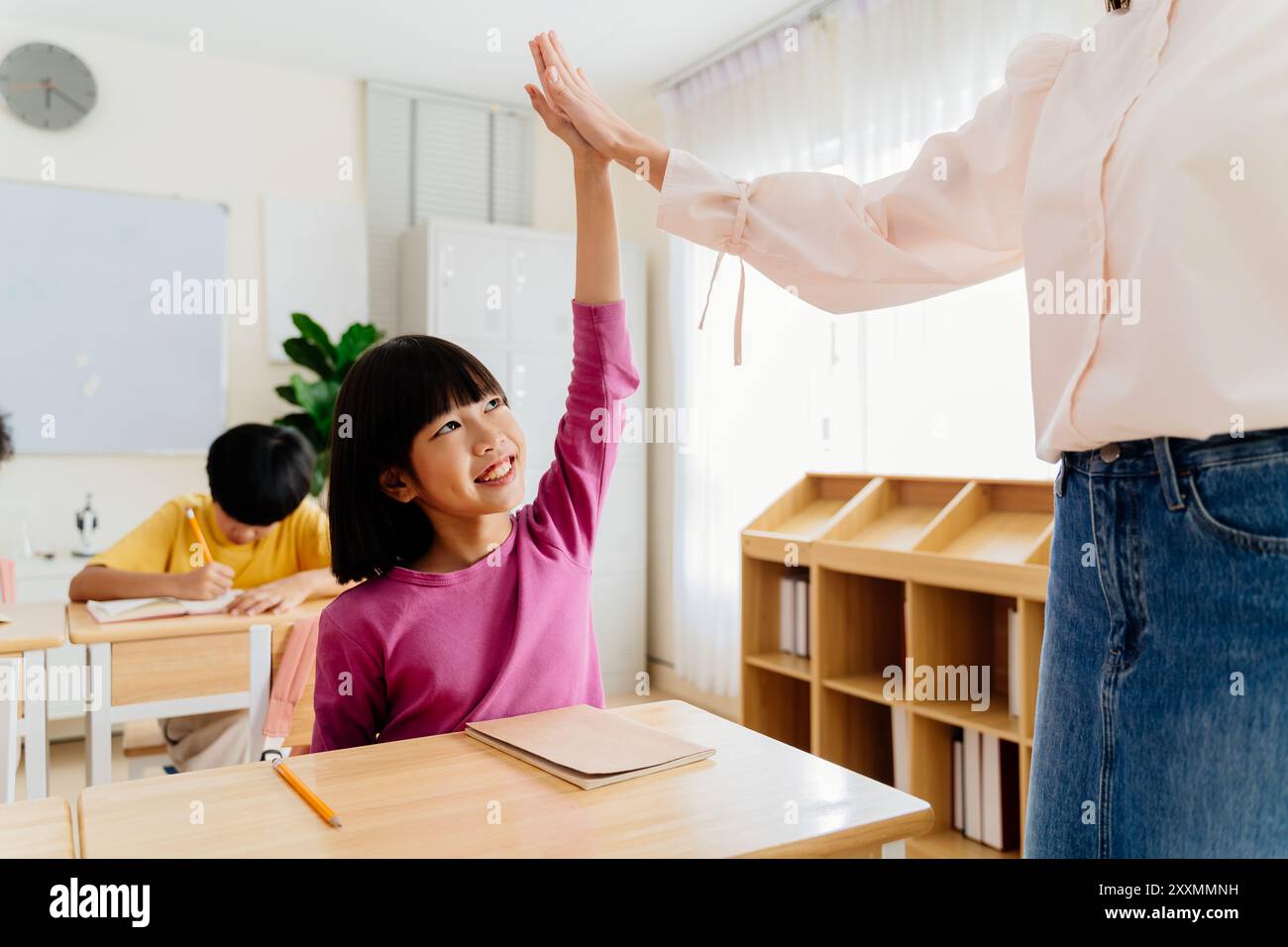 Joyful Asian primary student celebrating achievement with teacher ...