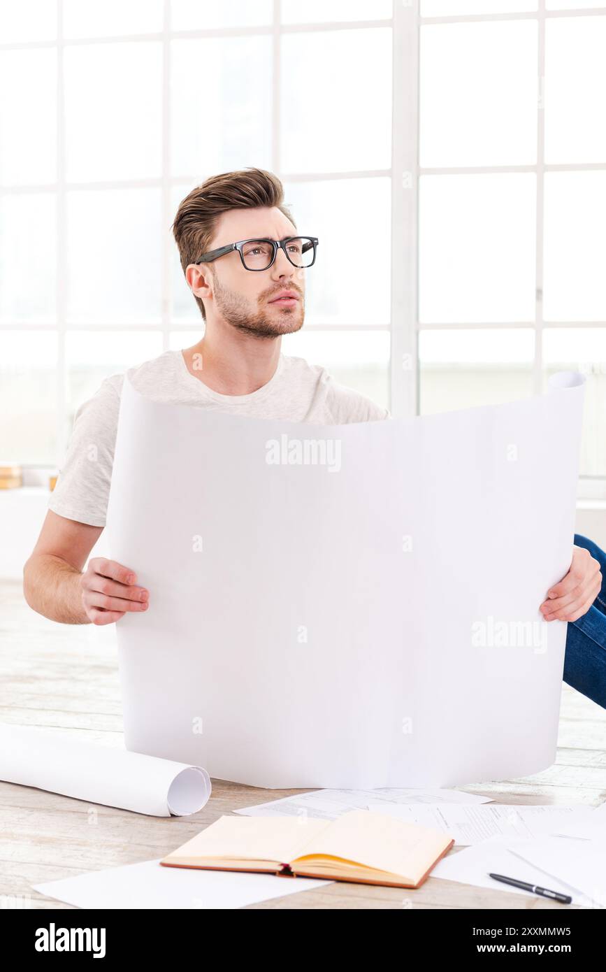 Thinking about new project. Thoughtful young man examining blueprint ...