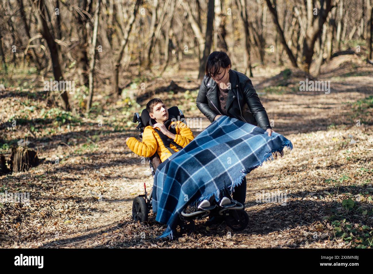 Mother caring for child in wheelchair during outdoor walk in forest ...