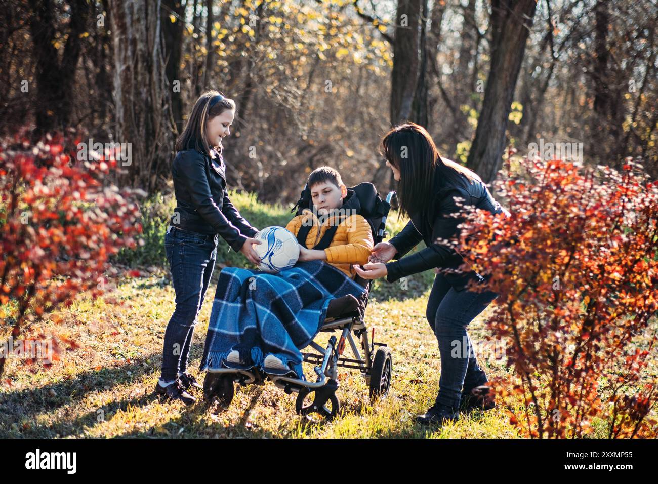 Mother and sibling engaging child in wheelchair in outdoor play with ...