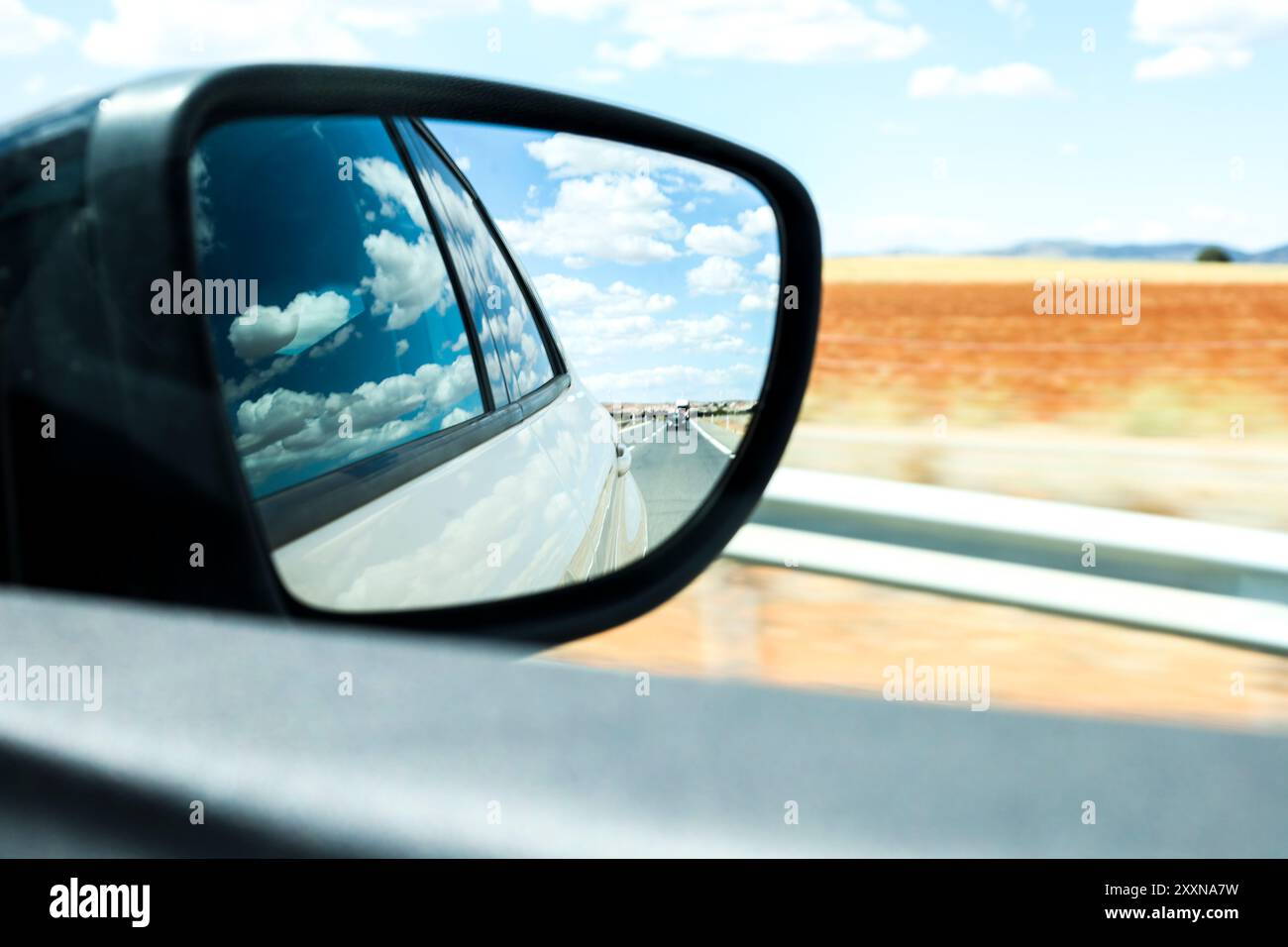 Car rearview mirror reflecting blue sky with clouds on the road in ...