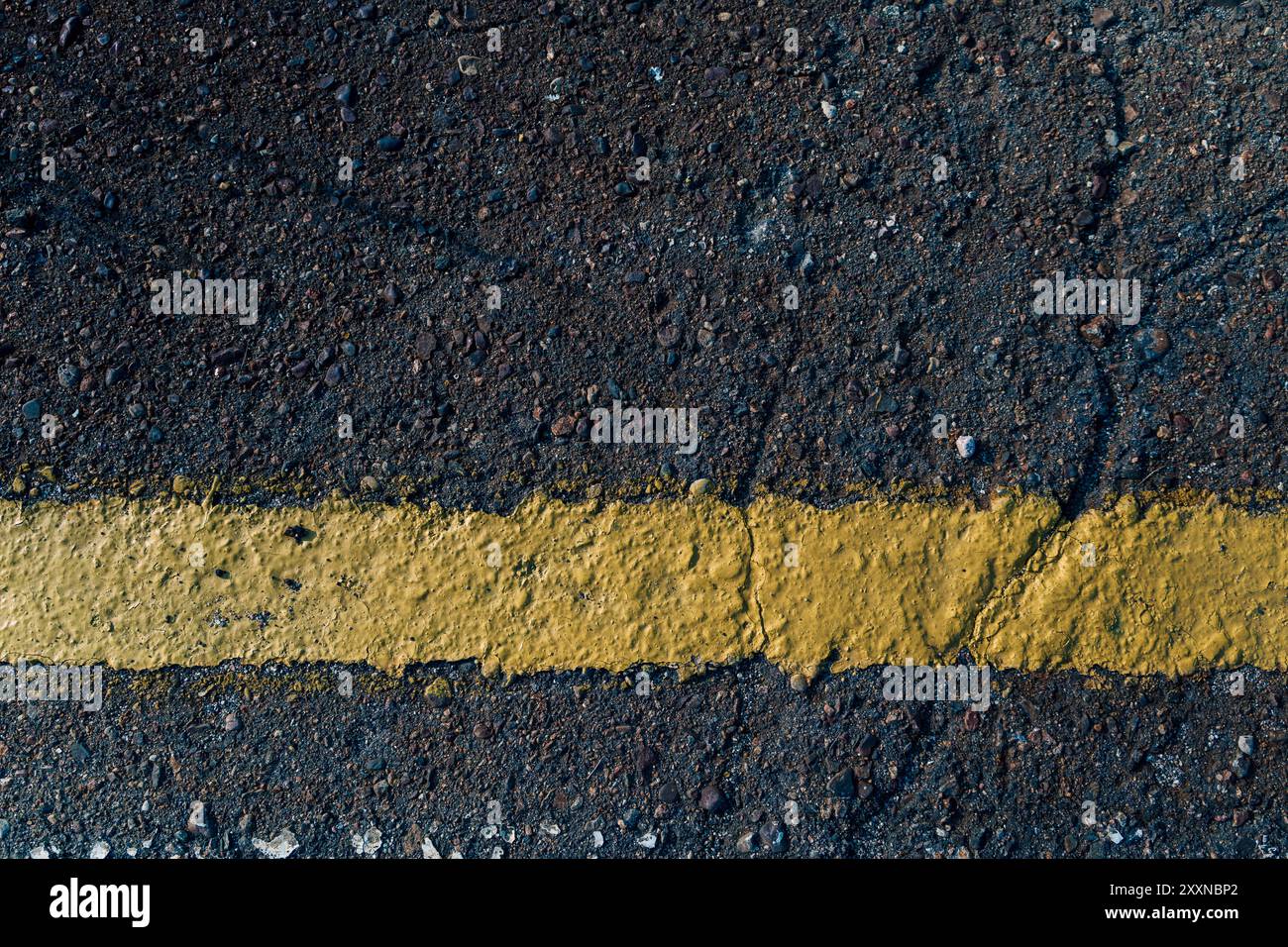 Close-up of an old, cracked asphalt road with a weathered yellow line ...