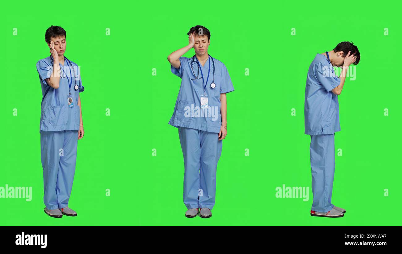 Unwell nurse suffering from a headache against greenscreen backdrop, wearing scrubs and feeling ...