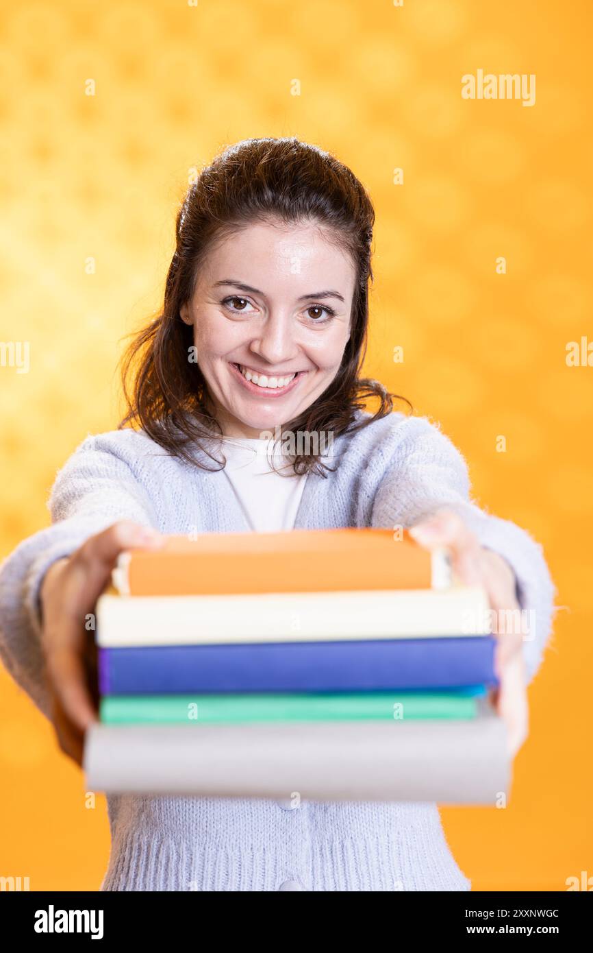 Portrait of joyous reading enthusiast woman offering stack of books ...