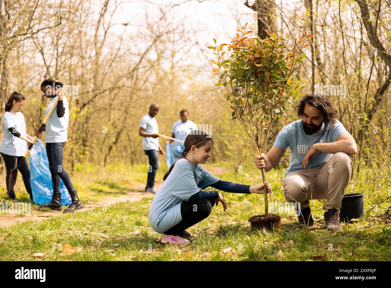 Man and young kid volunteering to fill a hole with a tree, working on ...