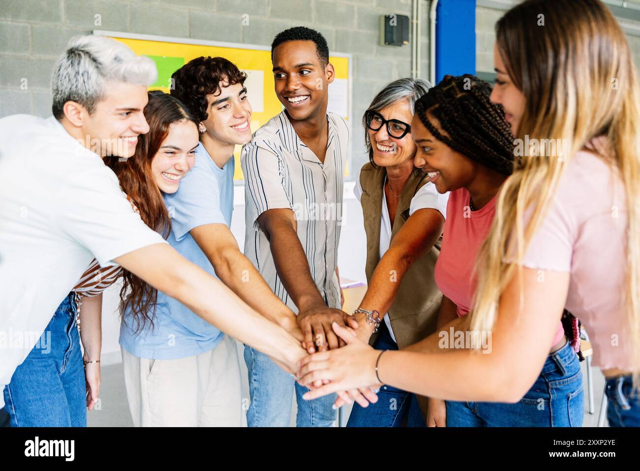 Diverse group of young students stacking hands with female teacher in ...
