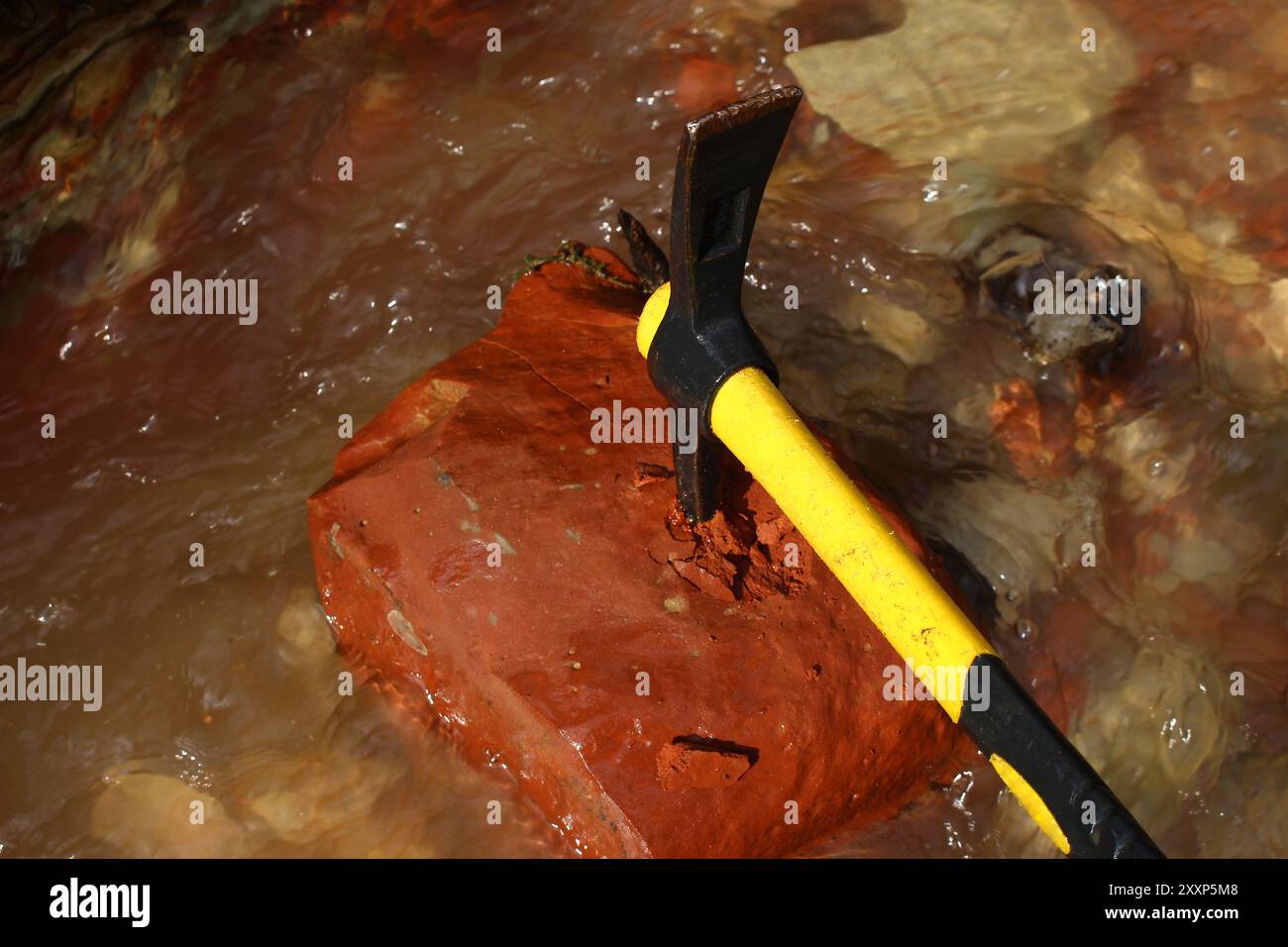 A pickaxe stuck into a piece of juicy red clay lying in a stream, raw ...