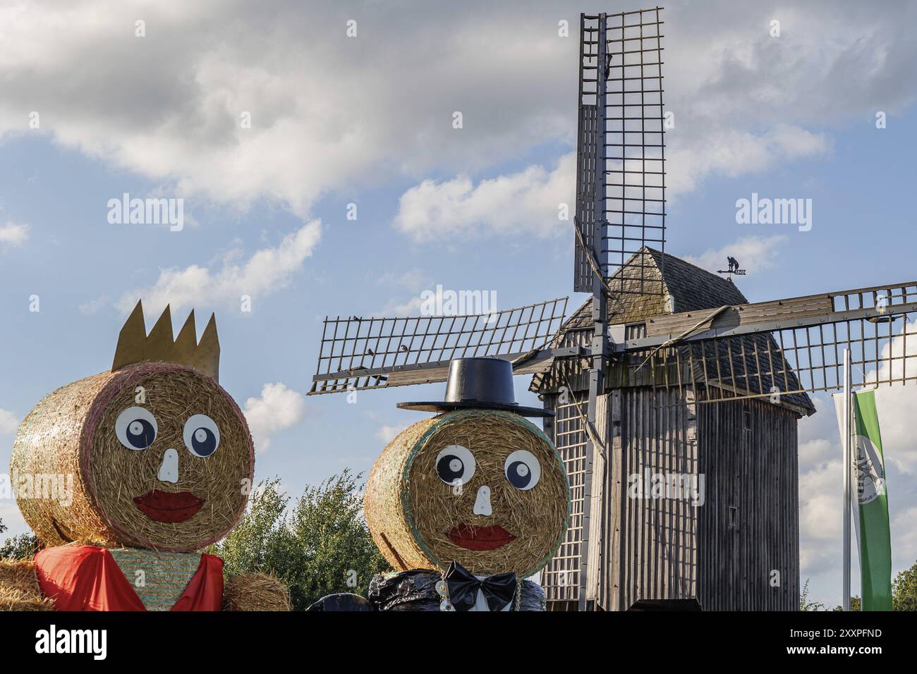 Cheerful straw dolls in front of an old windmill, one with a crown, the ...