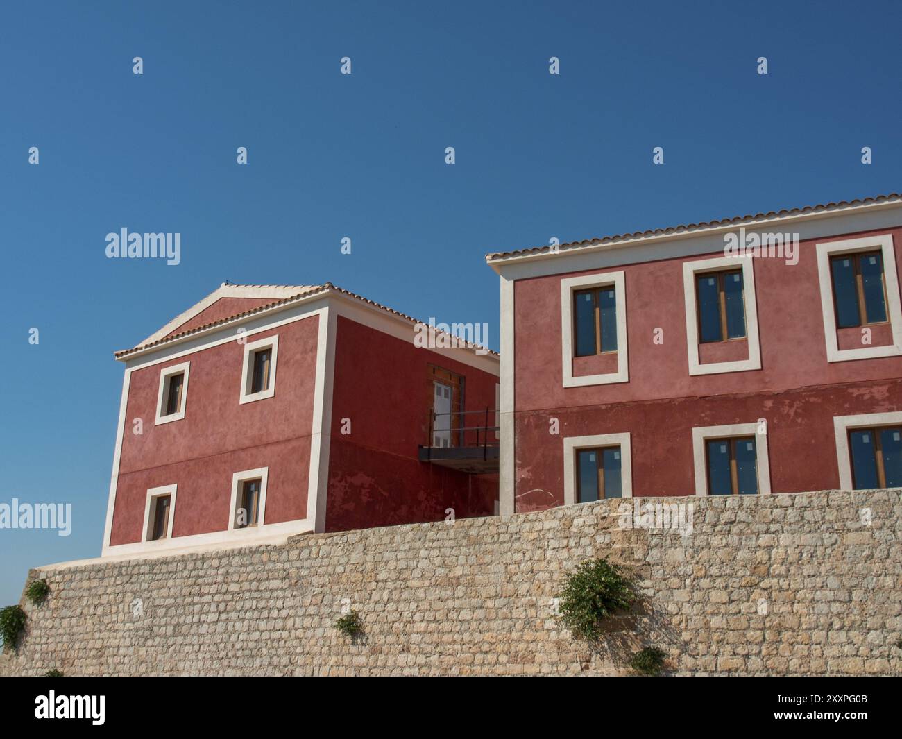 Two historic red buildings behind a stone wall, under a clear sky ...