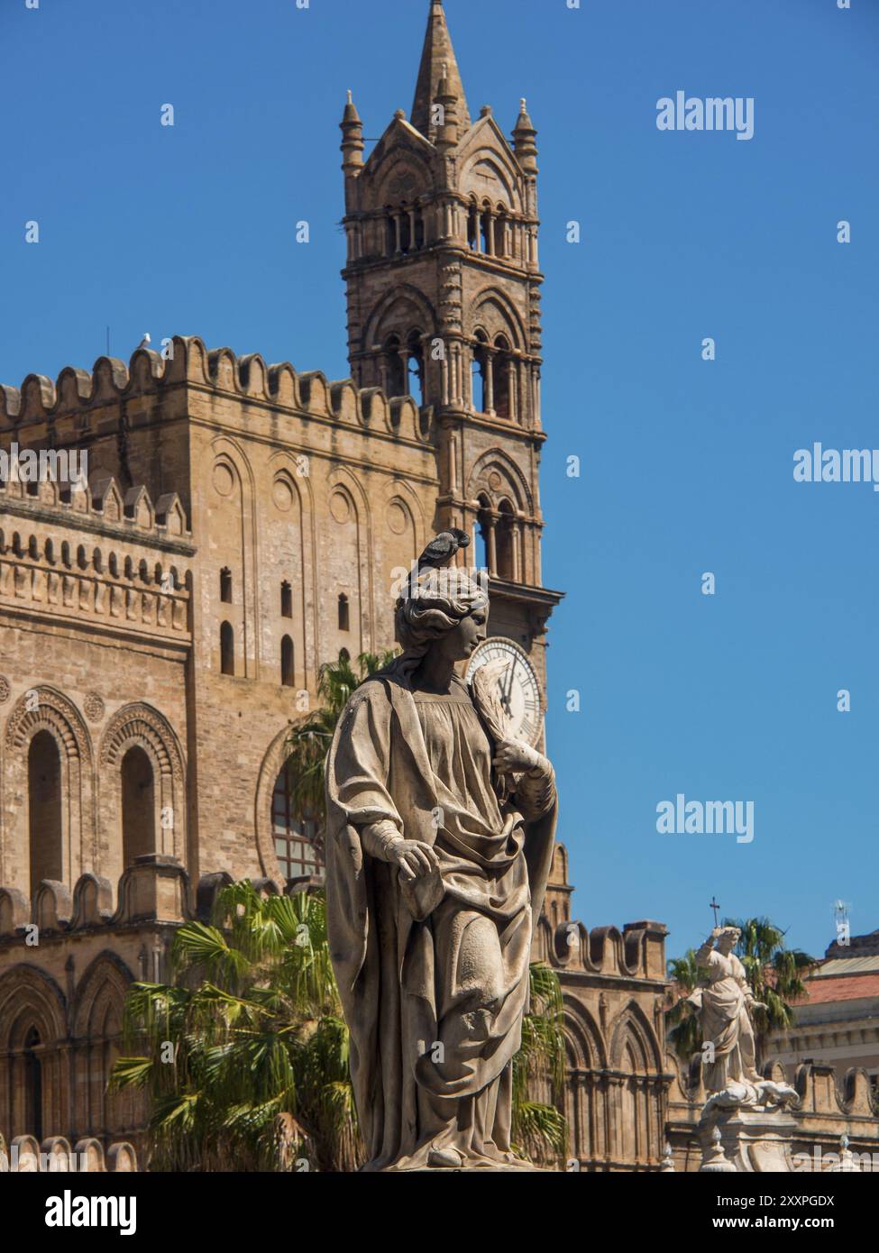 Statue in front of a gothic cathedral and a clock tower with palm trees ...