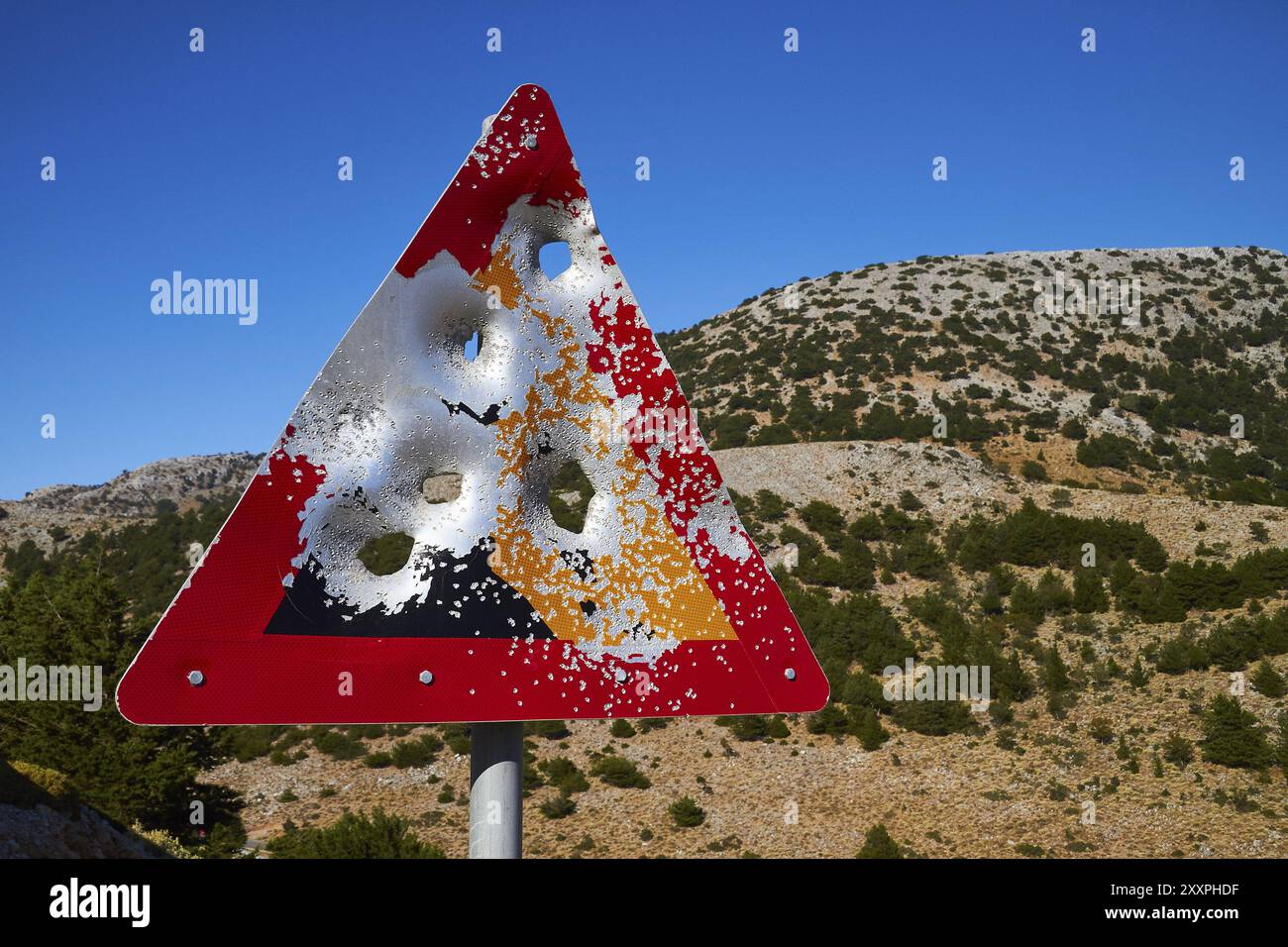 A damaged road sign with bullet holes in front of a mountainous ...