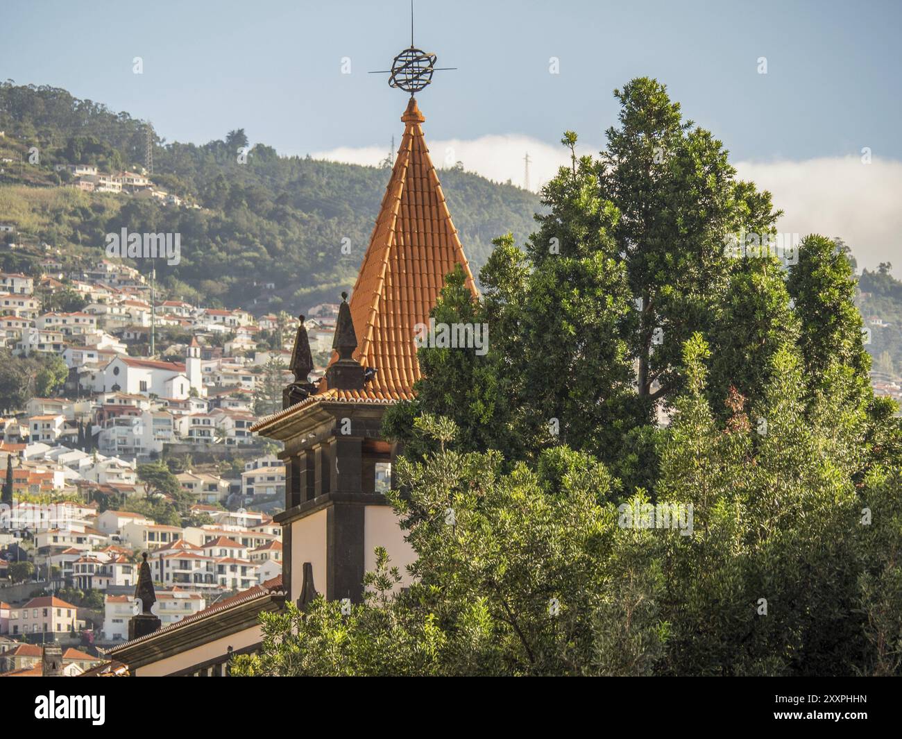 Top of a church tower with red roof rises above green trees, behind it ...