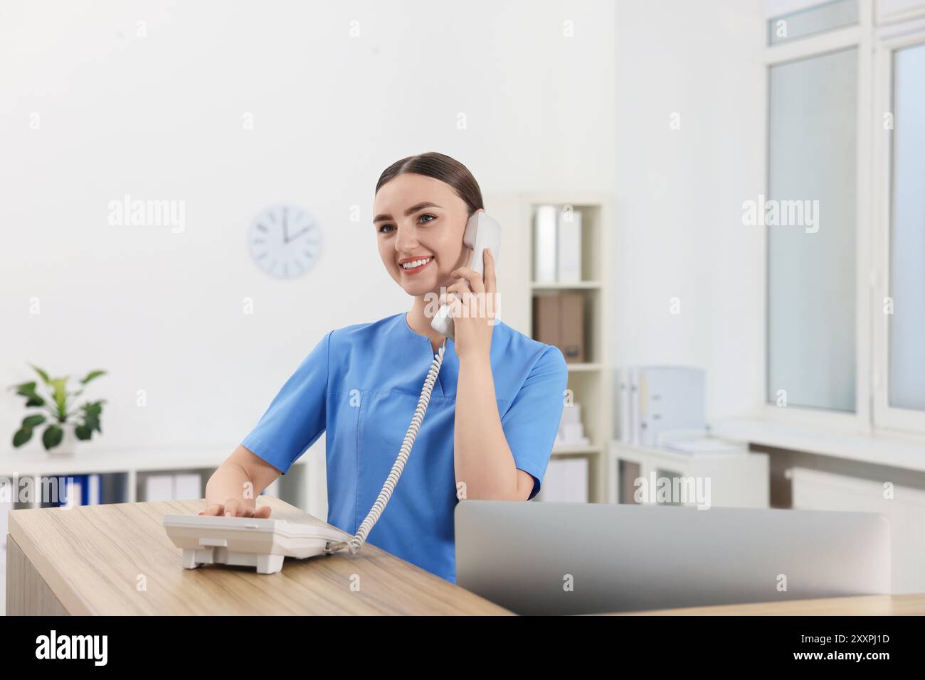 Professional receptionist talking on phone at wooden desk in hospital ...