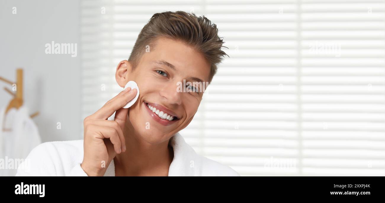 Handsome young man cleaning face with cotton pad in bathroom. Banner ...