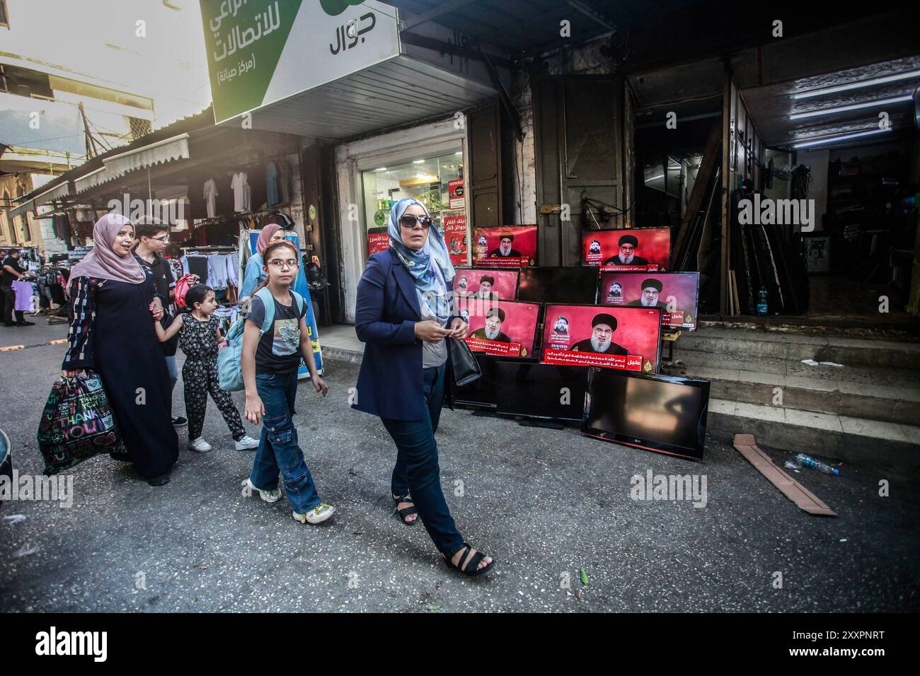 Nablus, Palestine. 25th Aug, 2024. Palestinians walk past tv screens ...