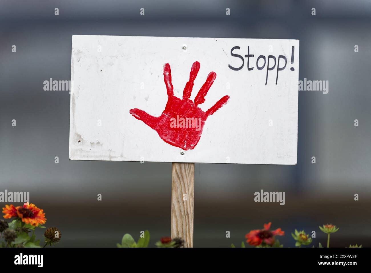 Sign with painted red hand stuck in a flower bed against a blurred ...