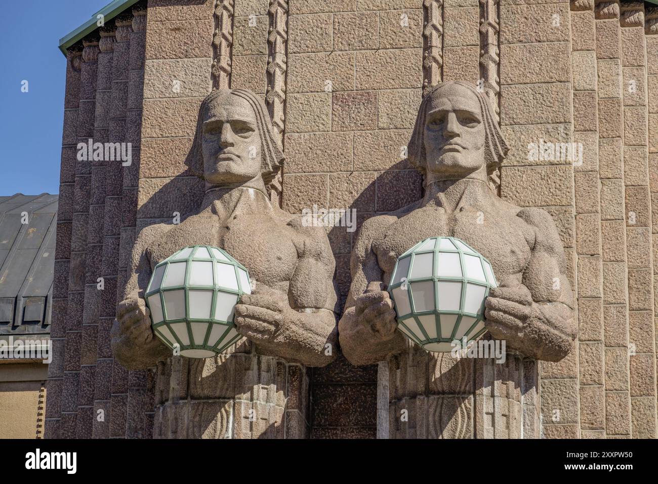 Two imposing male statues holding stylised lamps on a building ...