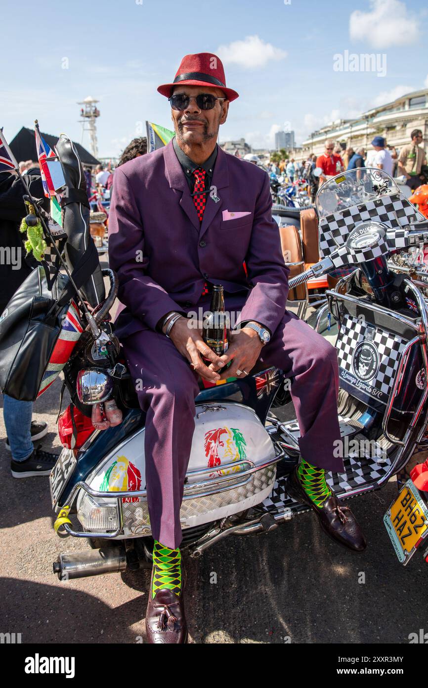 A man wearing a purple suit sits on a scooter. Thousands attend the ...