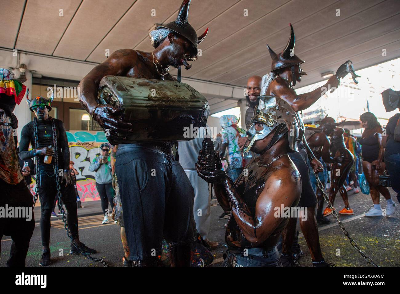 London, UK. 25th Aug, 2024. A Jab Jab character pours oil into the ...