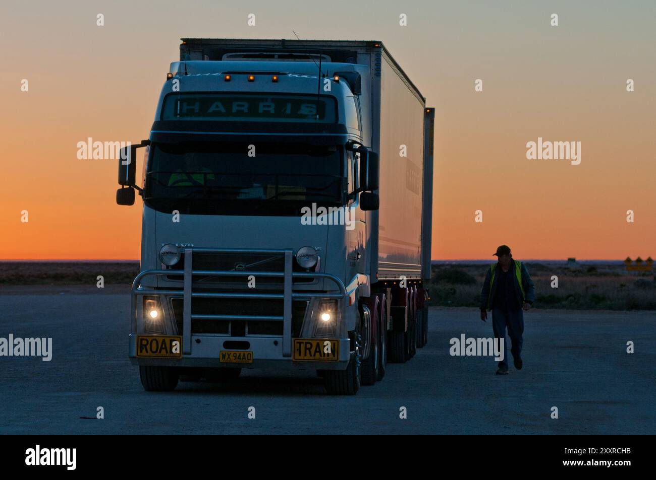 Road train at sunrise, driver checking the wheels on his rig before ...